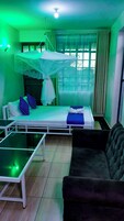 Quarto com cama, mesa de cabeceira, sofá e janela com cortinas.
