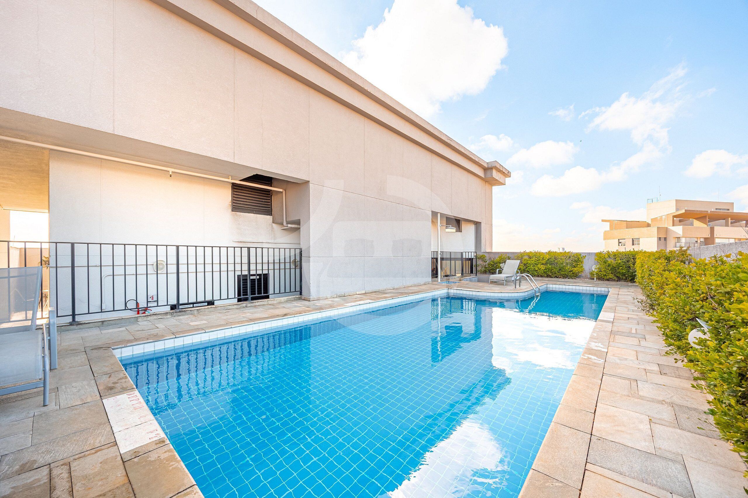 Um edifício moderno com piscina, área coberta e céu azul.