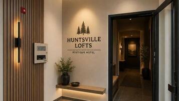 Um saguão de hotel com uma mesa de recepção, um alarme de incêndio fixado na parede, uma planta em vaso e uma placa para Huntsville Lofts Boutique Hotel.