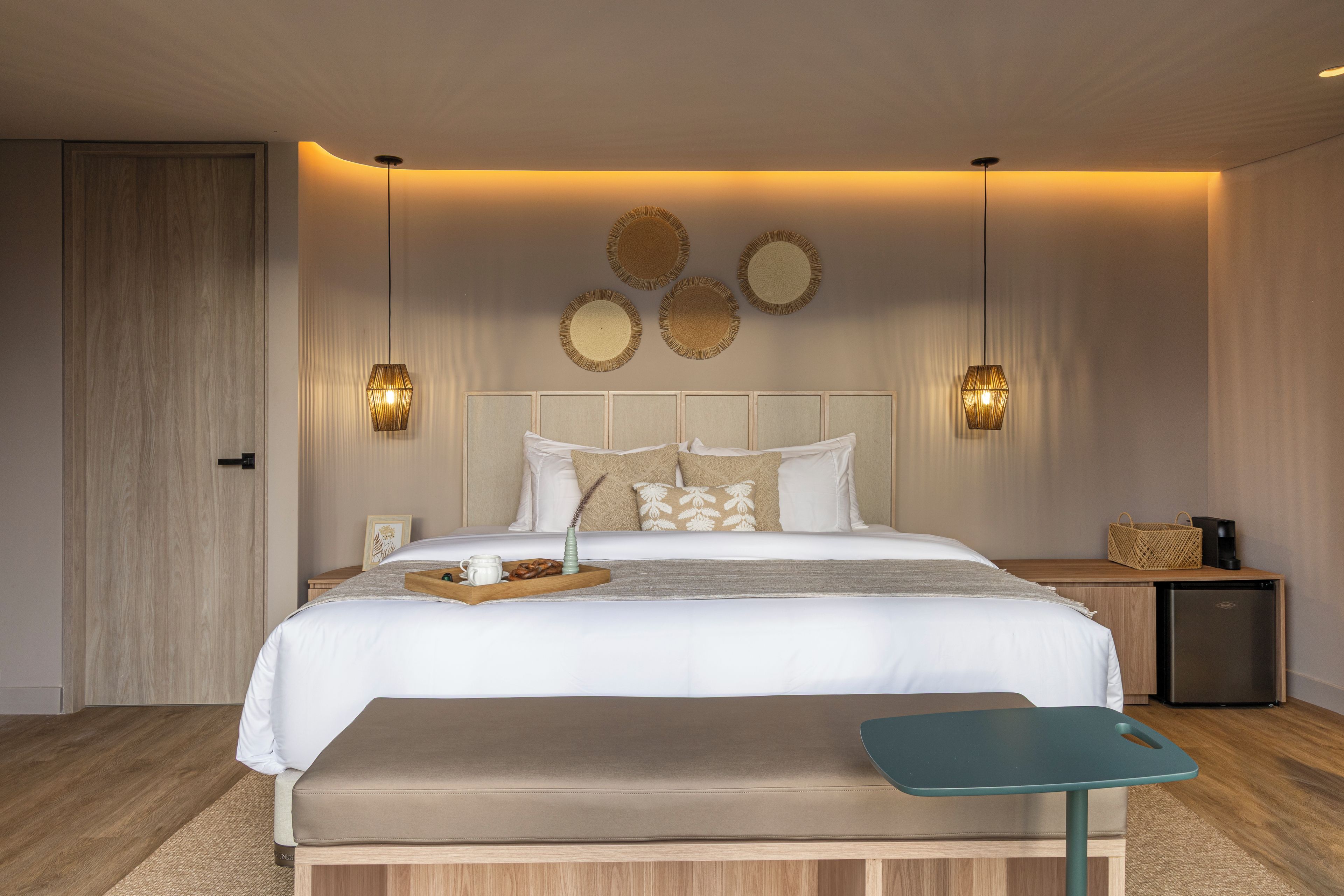 Quarto moderno com uma cama grande, mesas de cabeceira, um banco e arte decorativa na parede.