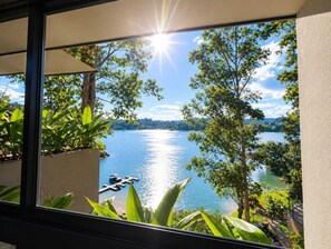 Vista de um lago sob um céu claro, rodeado por árvores e um edifício com varanda.