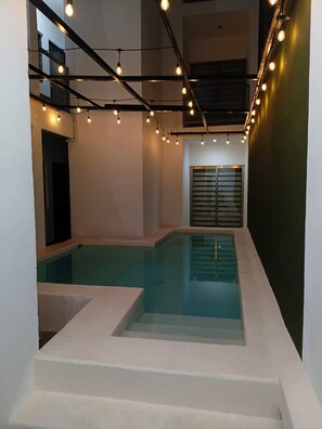Piscina com degraus para acesso, cercada por paredes e um teto com vigas aparentes e luzes de corda.