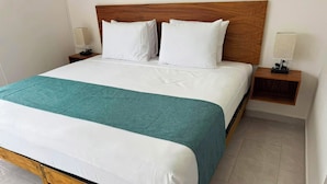 Uma cama com estrutura de madeira, roupa de cama branca e um cobertor azul-turquesa. Há duas mesas de cabeceira com abajures.