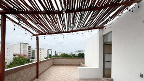 Terraço no telhado com piso estampado, pérgola de madeira e parede branca com porta.