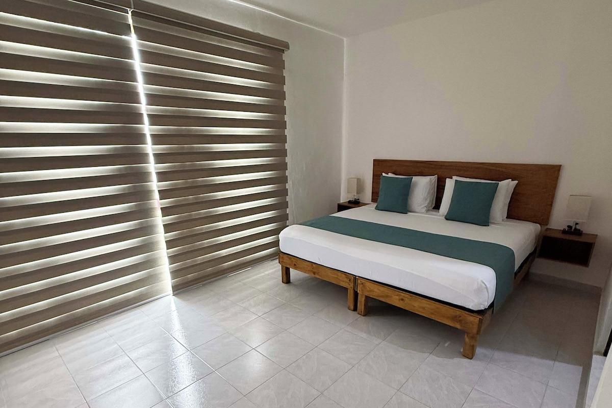 Quarto de hotel com cama, mesa de cabeceira e janela com persianas.