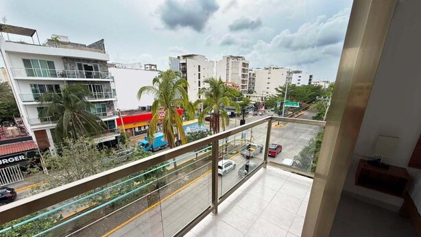 Varanda com vista para uma rua da cidade, incluindo edifícios e palmeiras.