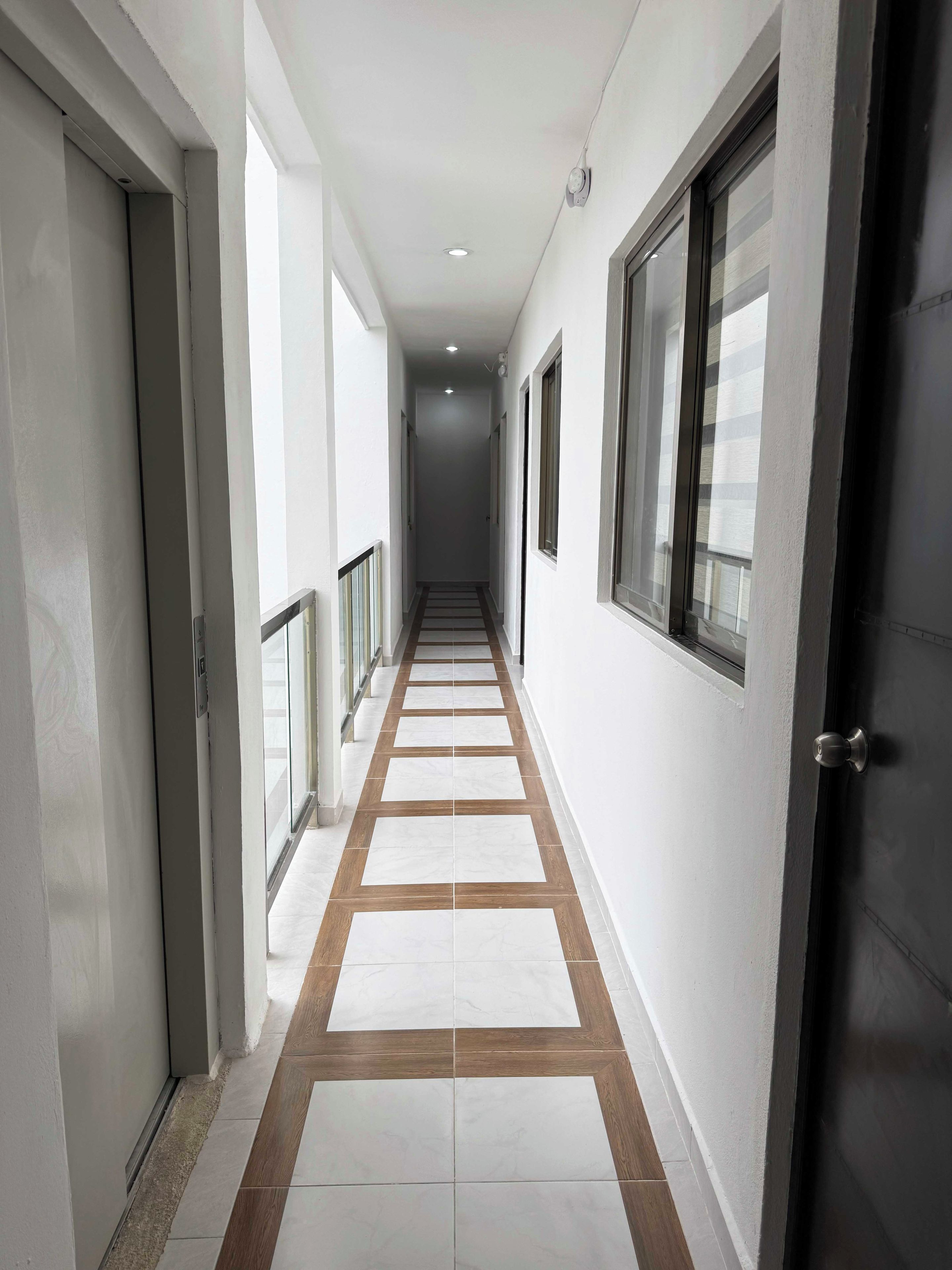 Um corredor com paredes brancas, chão de azulejos e uma porta à direita.