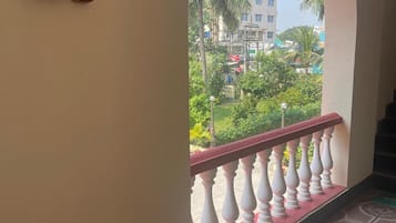 Uma varanda com vista para um edifício e vegetação, um relógio e um detalhe decorativo na parede.