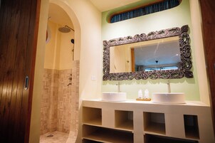 Casa de banho com chuveiro, duas pias e um espelho decorativo.