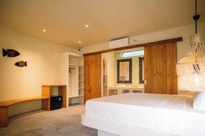 Quarto com cama, guarda-roupa de madeira, estantes embutidas, um banco e um enfeite de peixe na parede.