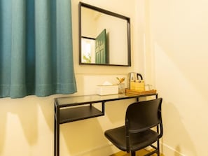 Quarto com escrivaninha preta, cadeira, espelho e janela com cortinas.