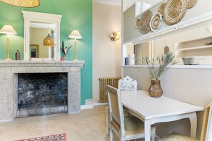 Uma sala de jantar com uma mesa e cadeiras brancas, lareira e arandelas decorativas.