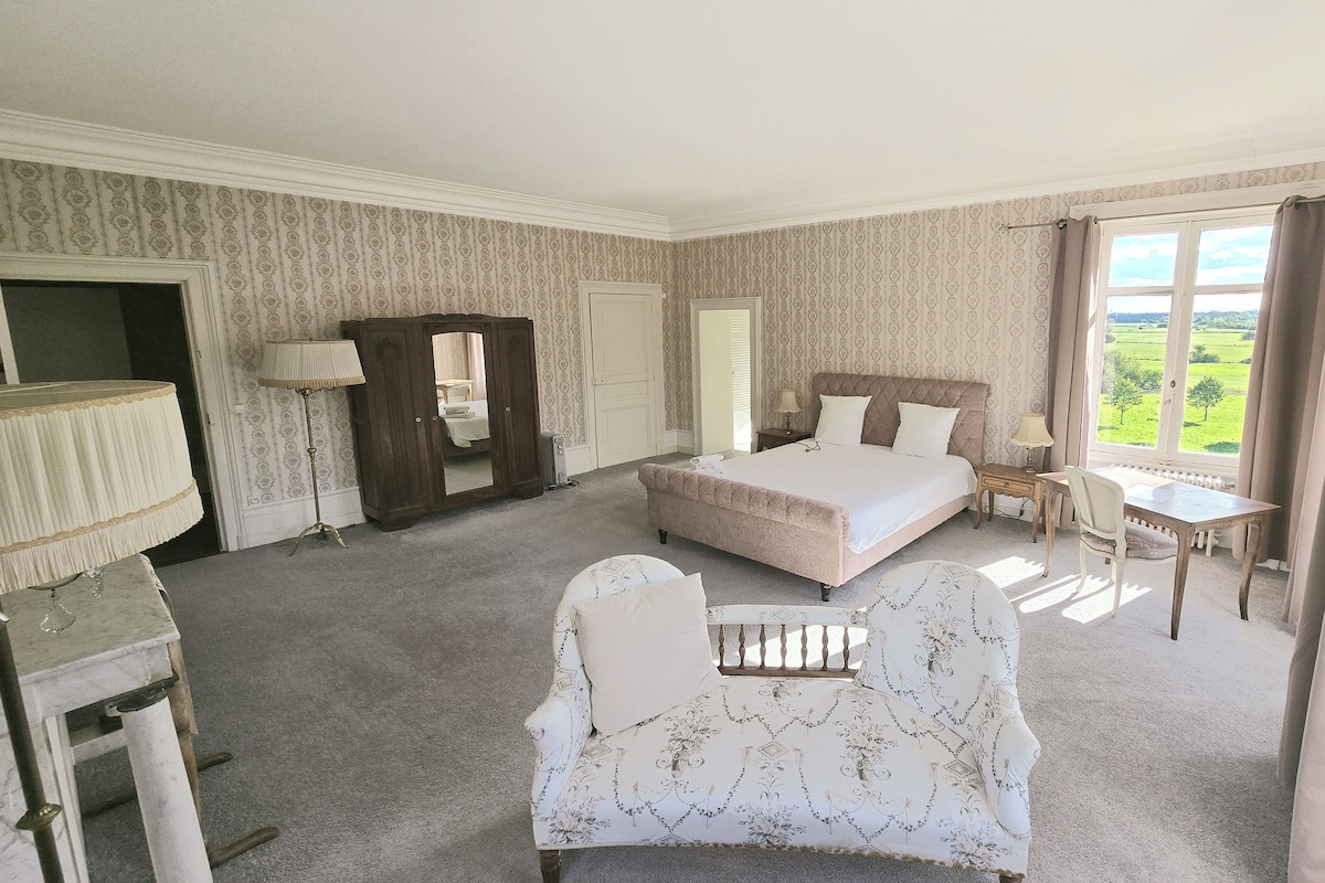 Quarto com cama grande, uma cadeira, escrivaninha e vista para o exterior.