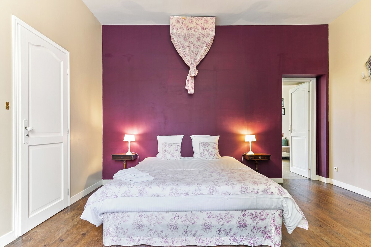 Um quarto com uma cama, duas mesas de cabeceira, uma luminária pendente e uma porta.