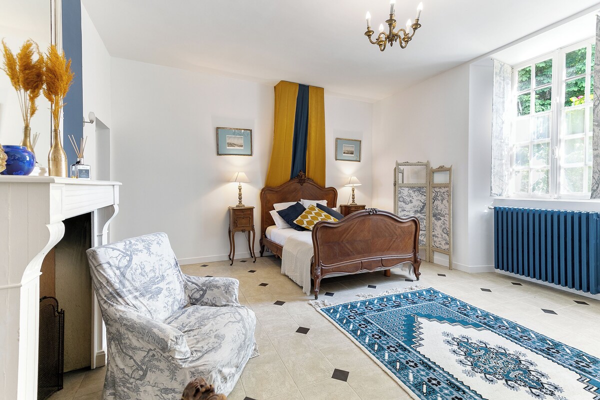 Quarto com cama, cadeira, lareira, janela e lustre.