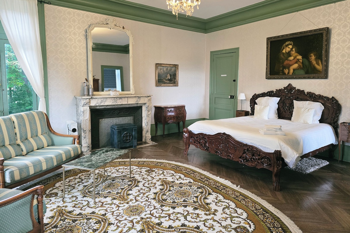 Quarto clássico com cama grande, lareira, espelho e um quadro na parede.