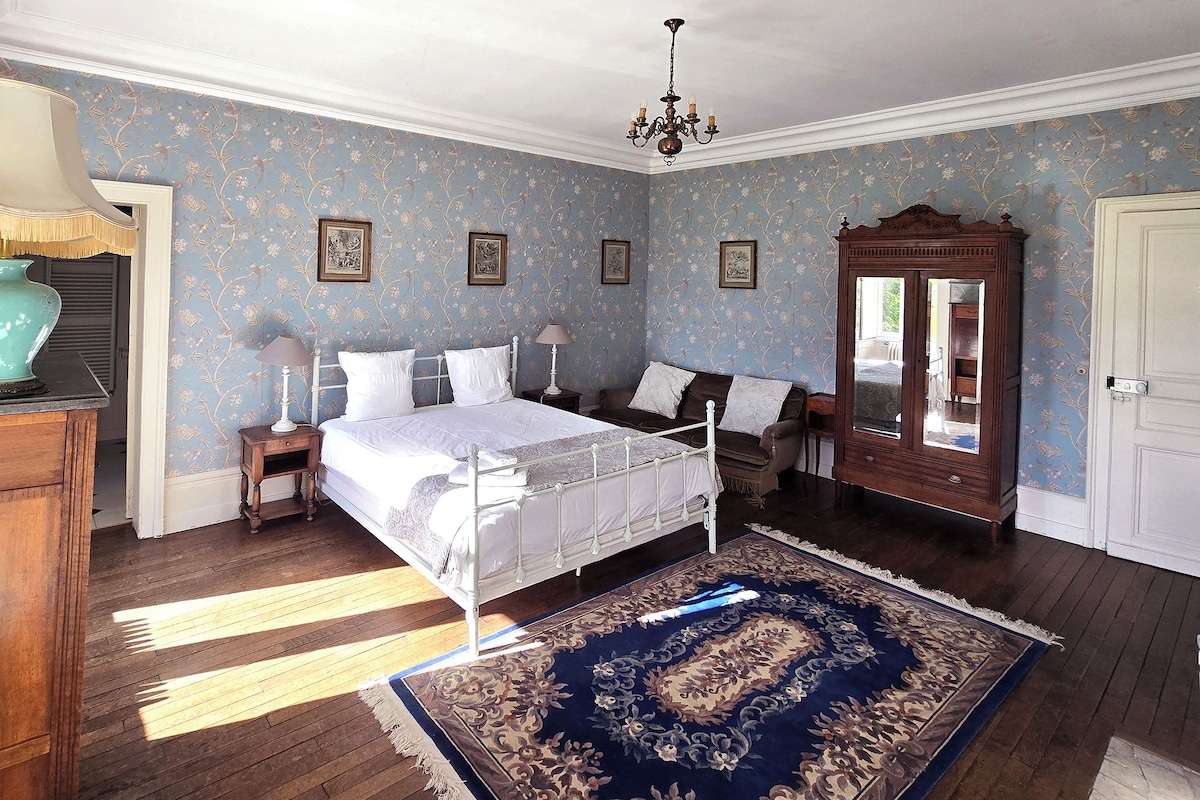 Quarto com cama de dossel, penteadeira de madeira, espelho e tapete estampado.
