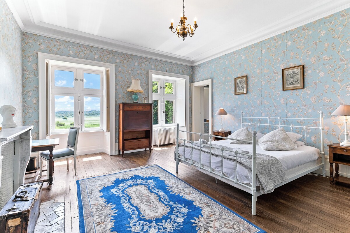 Quarto com uma cama grande, uma escrivaninha, uma cadeira e vista para o exterior através de uma janela.