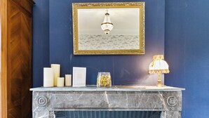 Uma lareira de mármore com um espelho emoldurado acima, um abajur decorativo e várias velas em cima do parapeito.