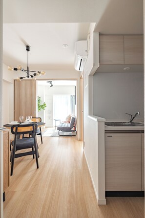 Cozinha moderna com lava-louças embutida, área de refeições com mesa e cadeiras de madeira, e sala de estar com sofá e planta.