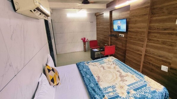 Quarto de hotel com cama, televisão na parede, uma cadeira vermelha e uma mesa pequena.