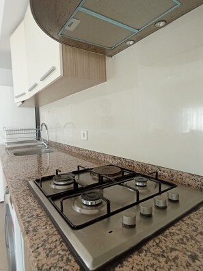 Cozinha com fogão a gás, eletrodomésticos em aço inoxidável e bancada de granito.