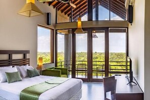 Quarto com cama grande, escrivaninha e varanda com vista para a paisagem.