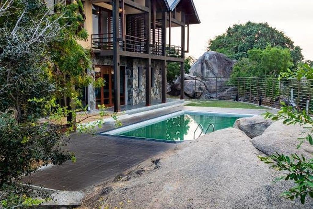 Um edifício moderno de dois andares com piscina, cercado por formações rochosas naturais e vegetação.