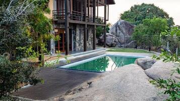 Um edifício moderno de dois andares com piscina, cercado por formações rochosas naturais e vegetação.