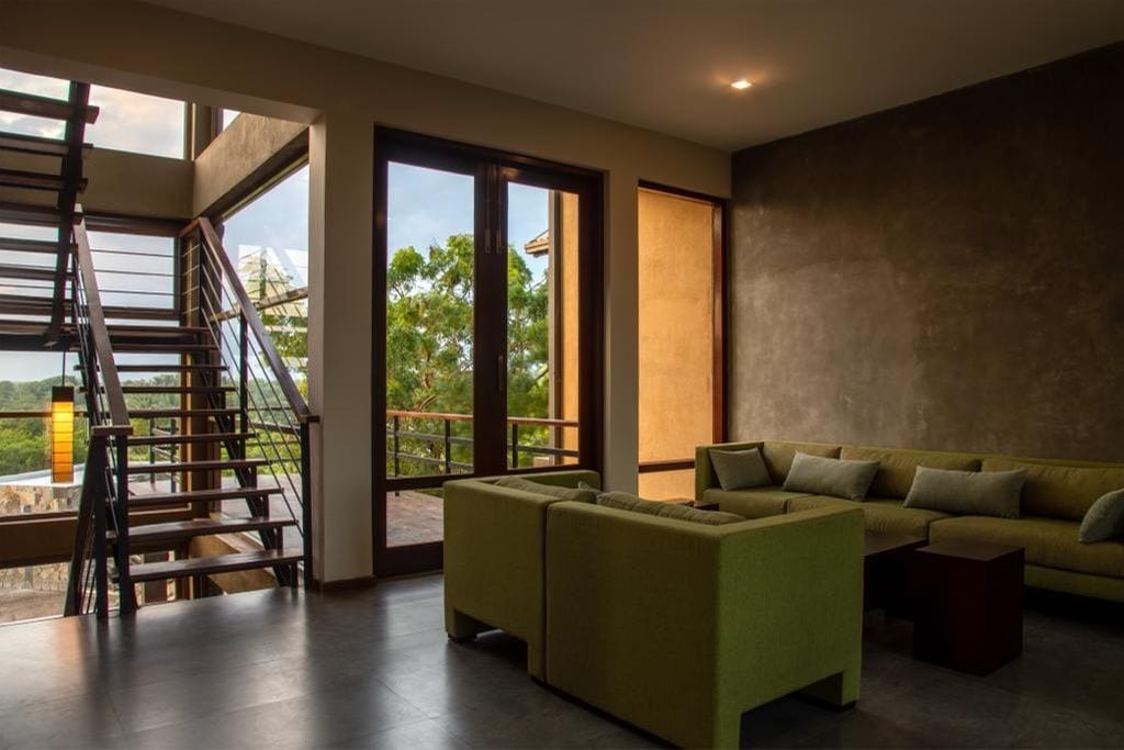 Sala moderna com escada, sofá e vista para o verde lá fora.