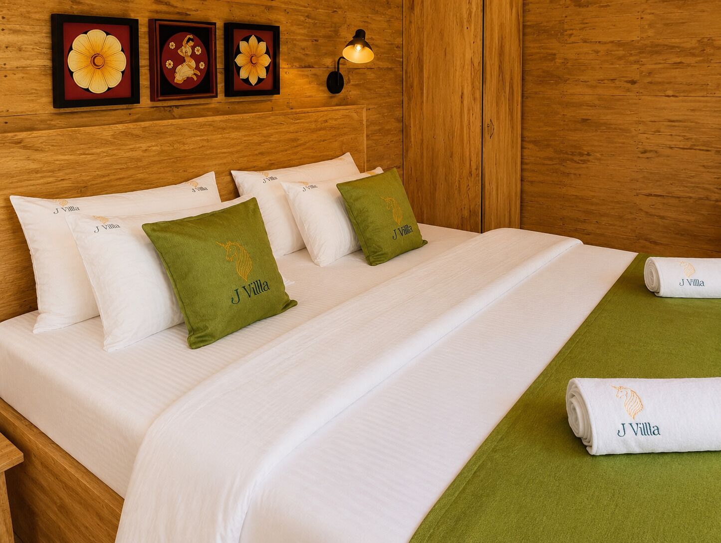 Cama bem arrumada com lençóis e almofadas brancos, um cobertor verde e uma toalha com logotipo.