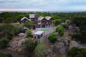 Edifício de vários andares com piscina, cercado por paisagem natural com rochas grandes e vegetação densa.