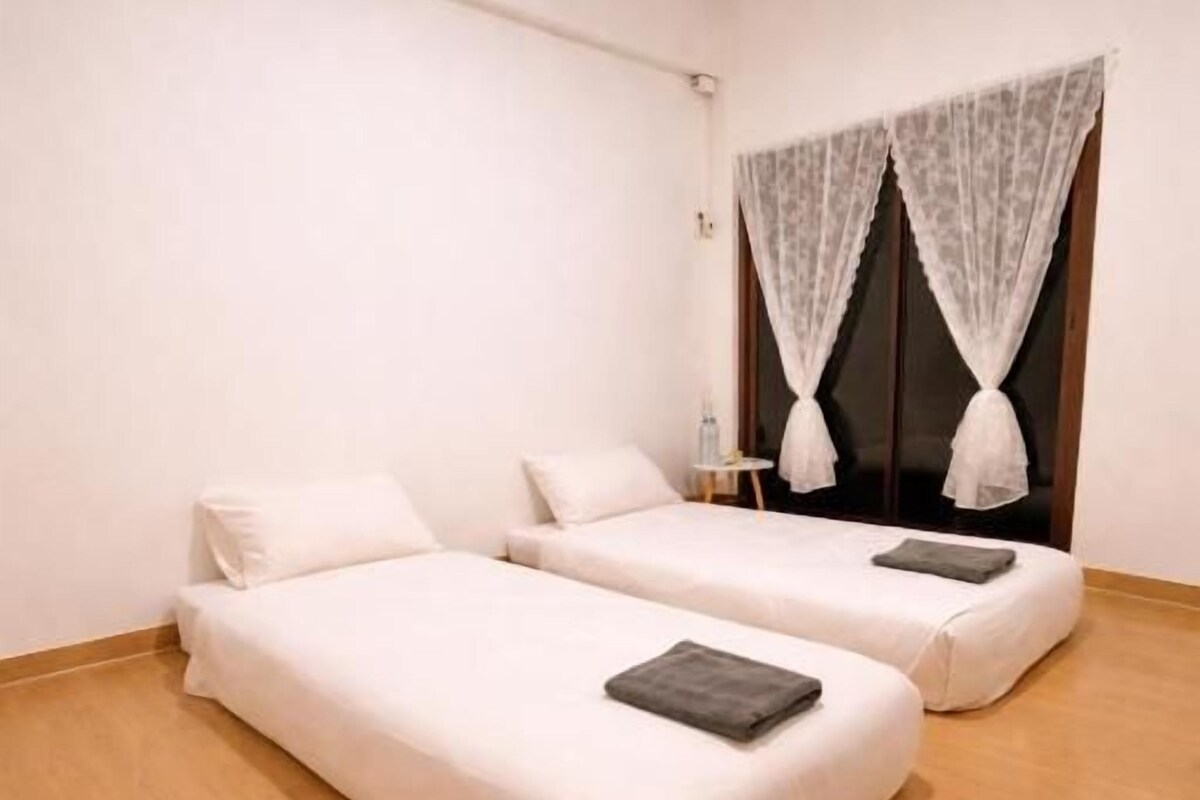 Quarto com duas camas, uma mesinha e janela com cortinas.