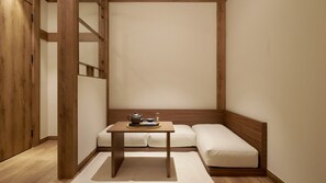 Quarto de canto com piso de madeira, sofá, mesinha com bule e xícaras, e parede branca.