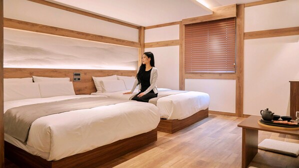 Quarto com duas camas, cabeceiras de madeira, mesa de cabeceira com bule e janela com persianas.