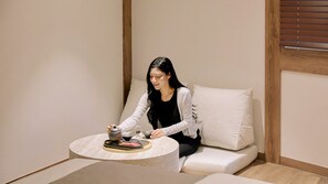 Uma pessoa sentada num sofá, com uma mesa à frente, segurando uma chaleira.