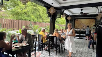 Área de refeições ao ar livre com mesas e cadeiras, cercada por vegetação e um muro de madeira.