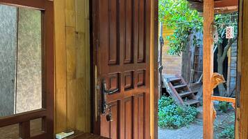 Uma porta de madeira com fechadura e puxador, dando acesso a uma área externa com escada de madeira e vegetação.