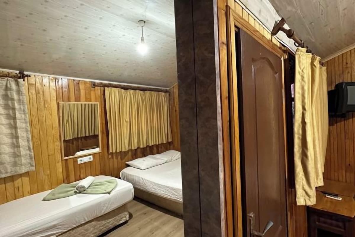 Quarto com duas camas, paredes de madeira, espelho, televisão e porta com cortinas.