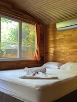 Quarto de cabana de madeira com uma cama, janela com cortinas e aparelho de ar condicionado.