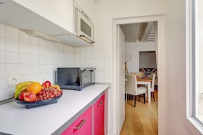 Cozinha com azulejos brancos, micro-ondas, torradeira e uma cesta de frutas na bancada.