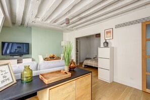 Uma sala moderna com televisão, área de jantar com mesa posta para dois e quarto com cama e guarda-roupa.