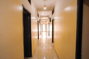 Corredor de hotel com portas em ambos os lados, piso de azulejos e luminária suspensa.