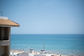 Vista costeira com céu limpo, praia e um edifício com telhado de azulejos.
