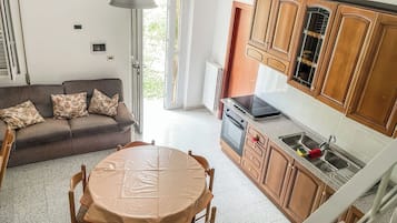 Um espaço de estar compacto com cozinha compacta, um sofá com almofadas estampadas e uma mesa de jantar com cadeiras.