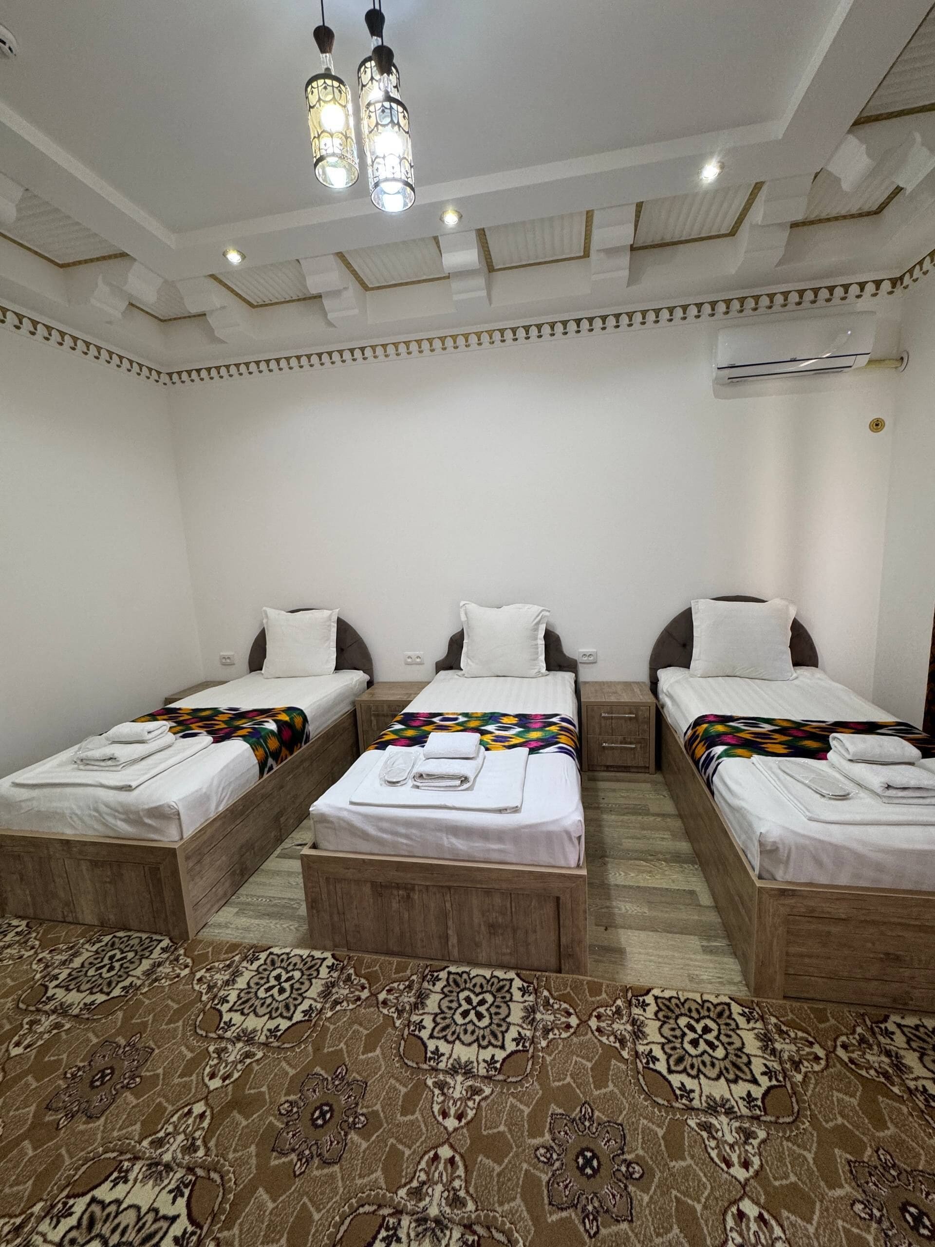 Quarto de hotel com três camas, carpete estampado e ar-condicionado.