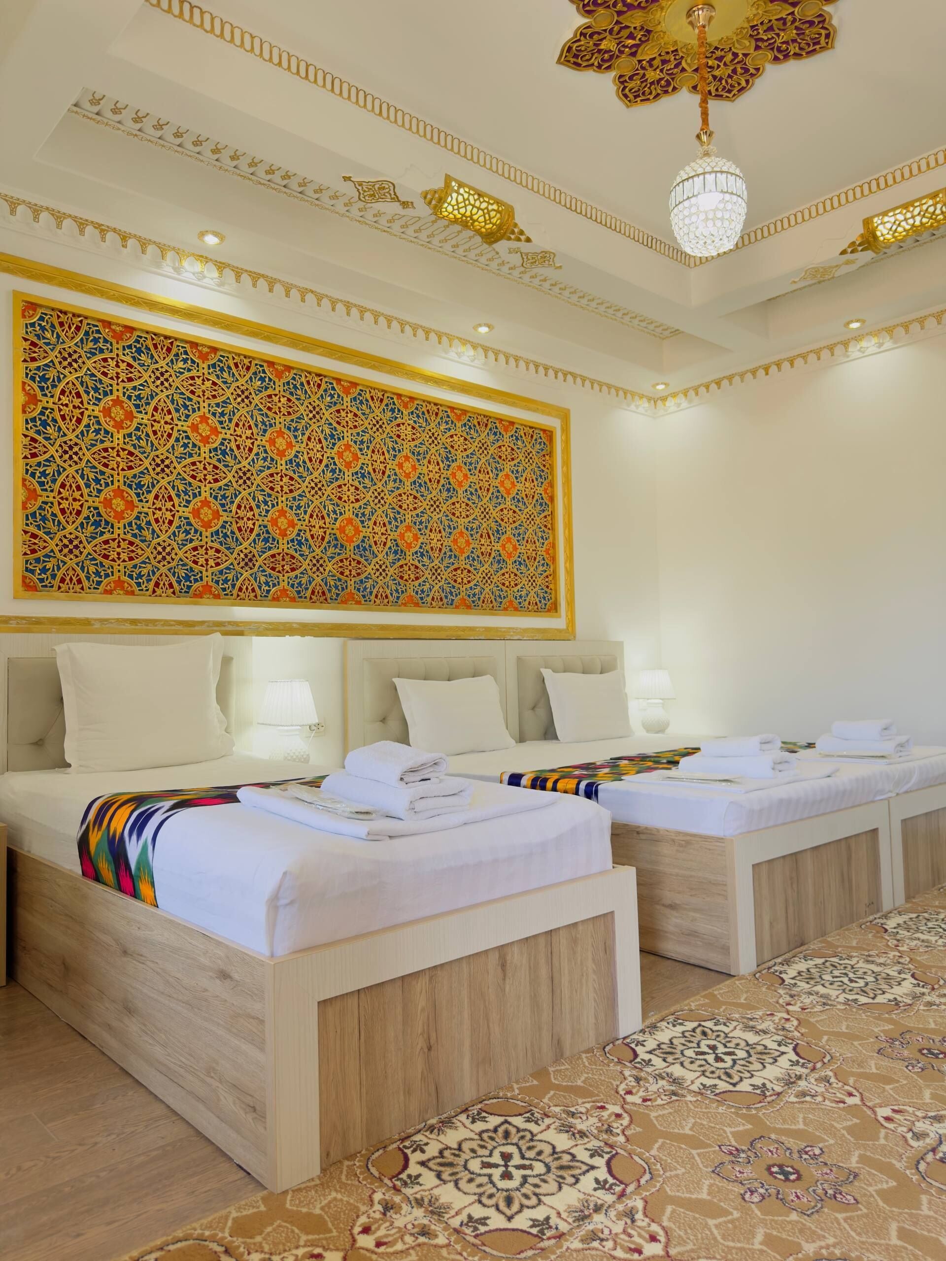 Quarto de hotel com duas camas, uma parede decorativa grande e um candelabro.
