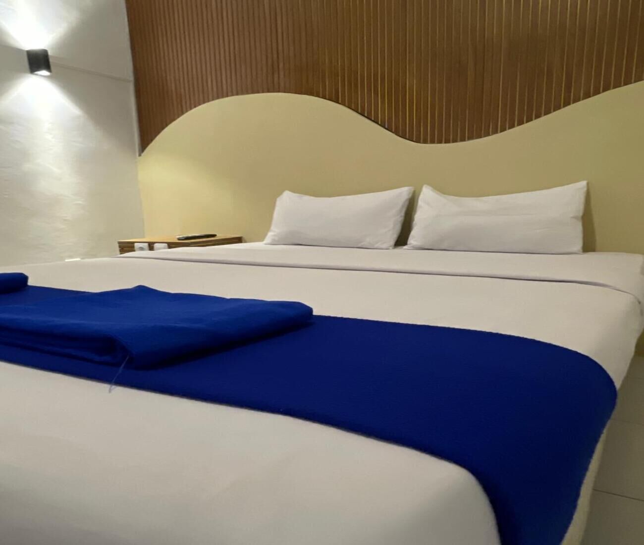 Quarto de hotel com cama, mesa de cabeceira e luminária na parede.