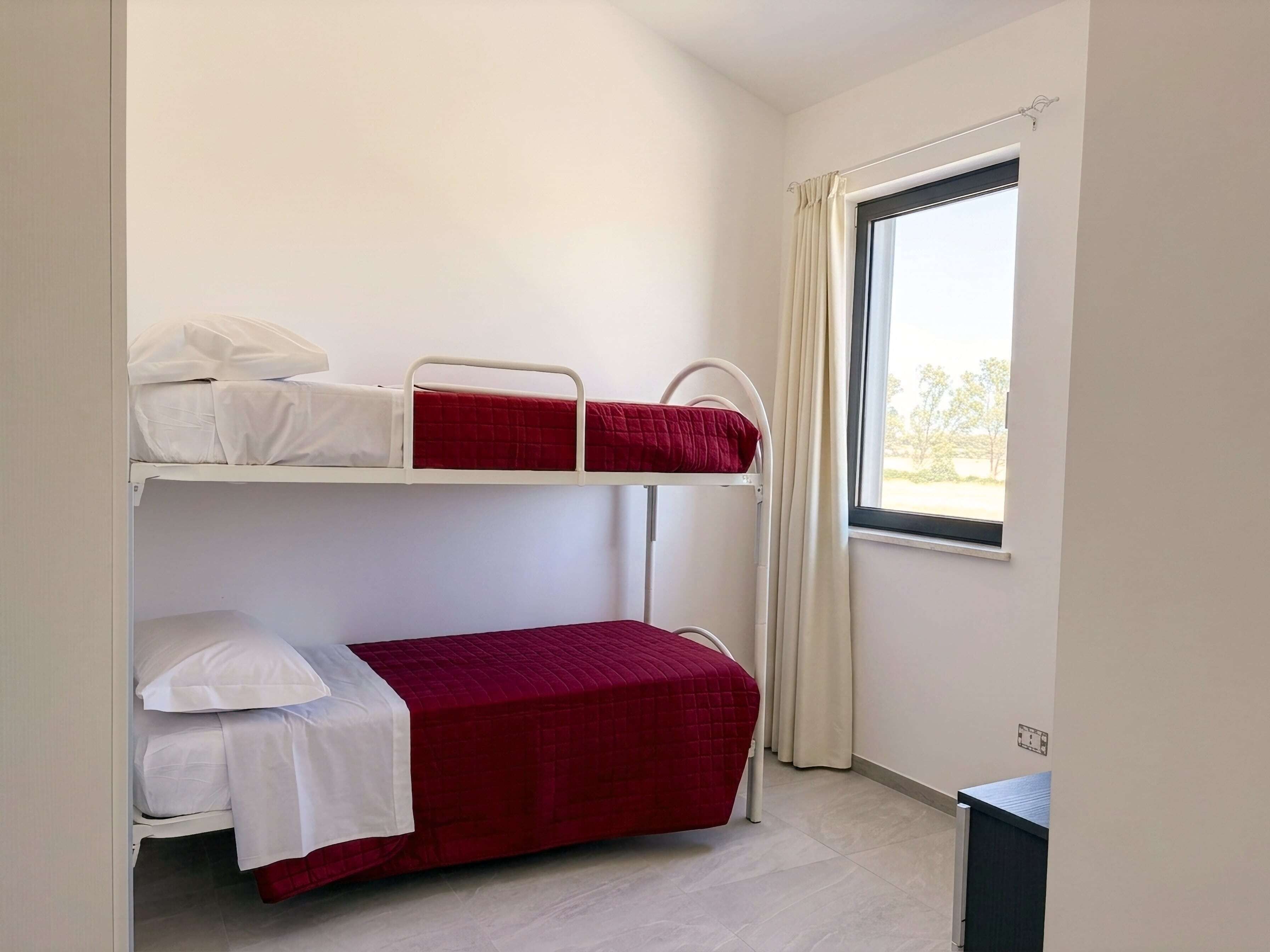 Quarto com beliche, janela e escrivaninha.