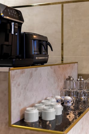 Máquina de café e conjunto de chá sobre bancada de mármore com moldura dourada.